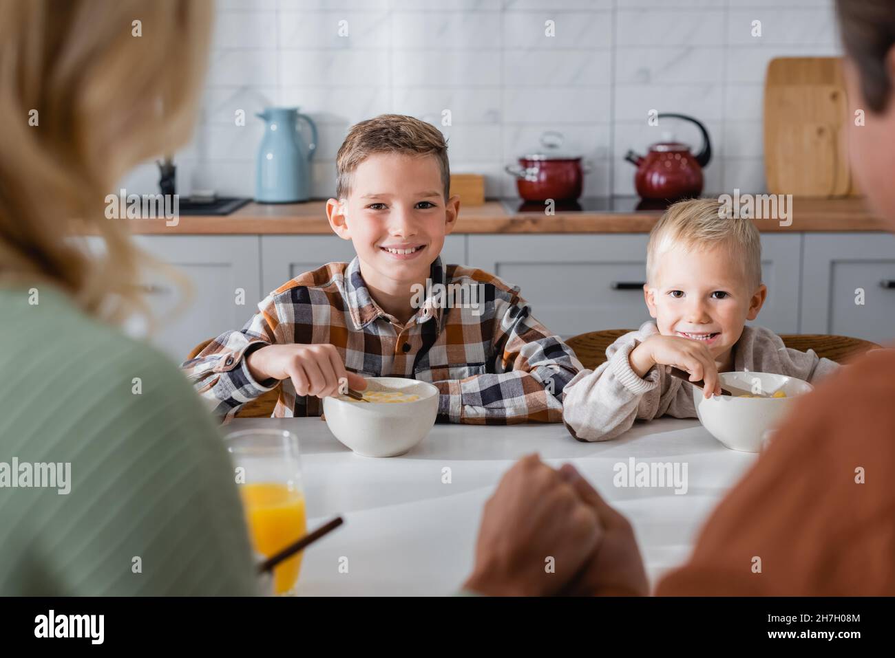 smiling boys eating delicious corn flakes near blurred parents in ...