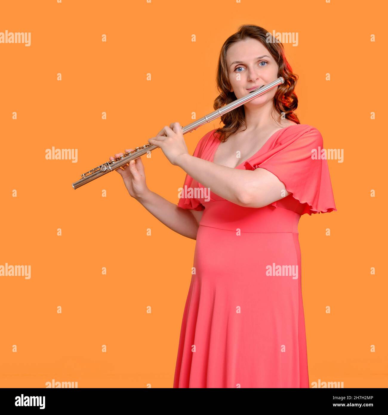 Portrait of a woman musician with a flute on a studio yellow background ...