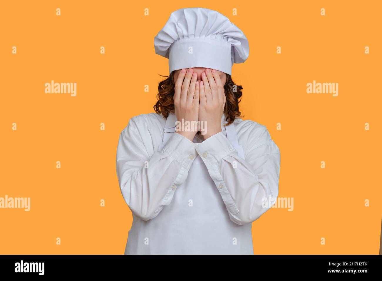 Woman chef crying with her hands to her face on studio background ...