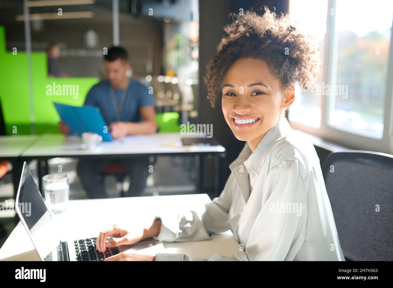 Young curly-haired female office worker sittin at the table in the ...