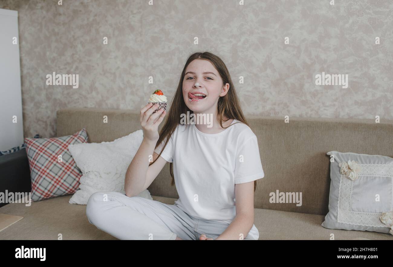 a young girl eats a delicious cupcake smeared with cream sitting at ...