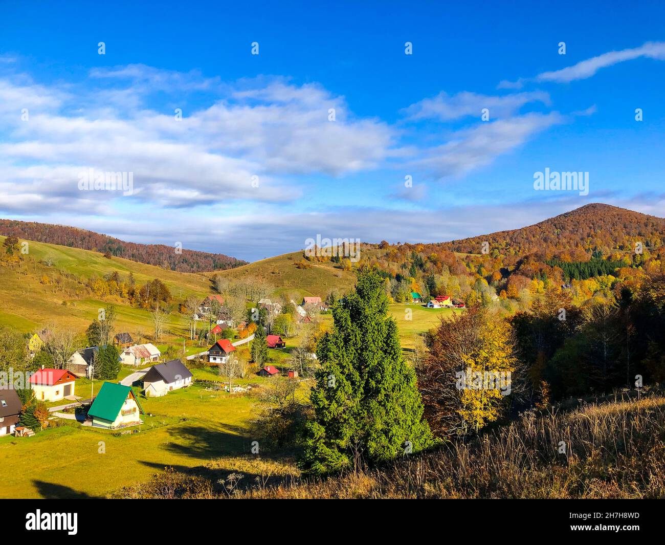 Colorful autumn trees in the beautiful meadow with hills and the blue ...