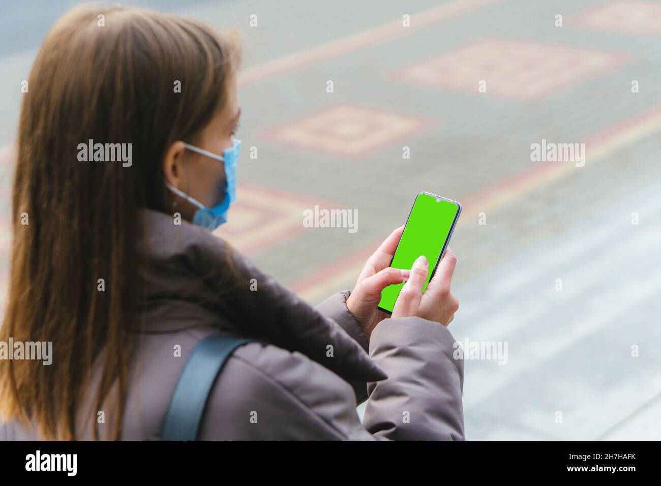 Woman in protective mask holding smart phone with blanck green screen ...