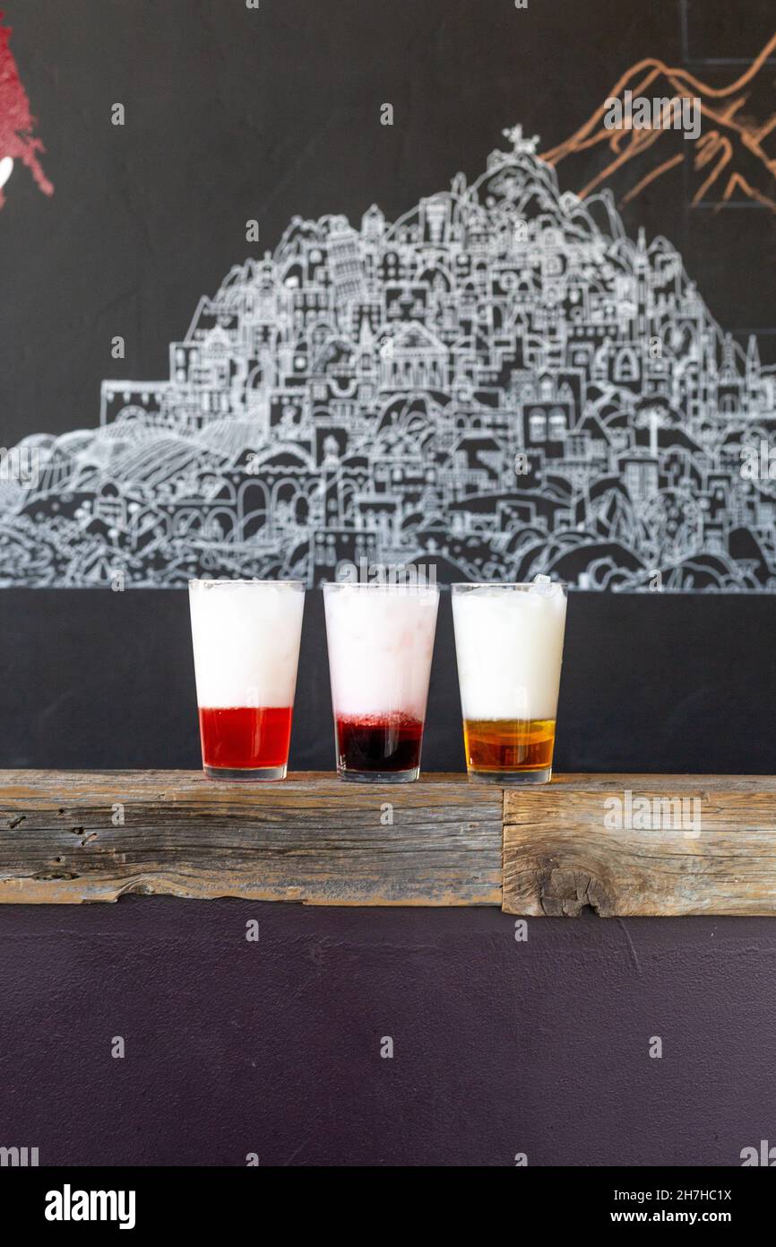 Red, yellow and purple beverages with ice and foam on wooden counter in ...