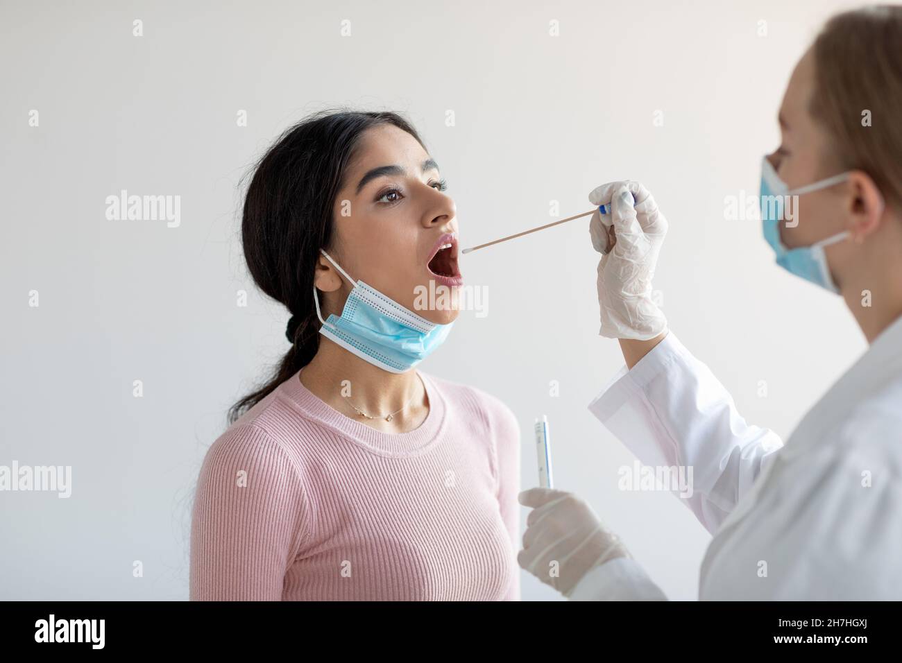 European doctor doing covid-19 pcr test for young indian woman on gray ...