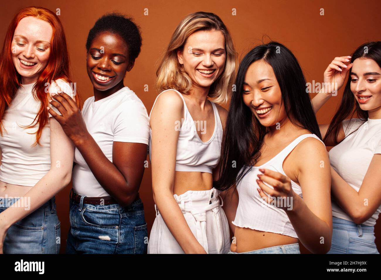 young pretty african and caucasian women posing cheerful together on brown background, lifestyle ...