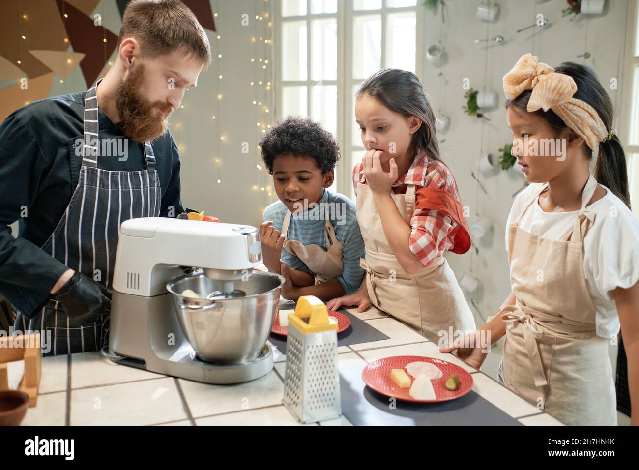 Man mixing the flour in mixer and children watching for the process of ...