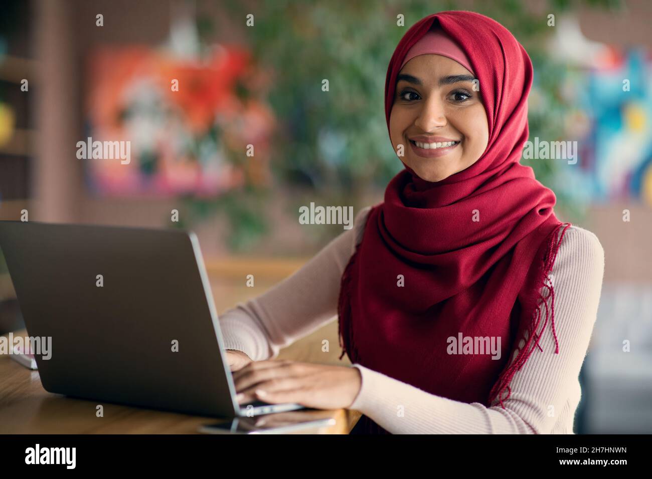 Religious muslim woman typing on computer keyboard, cafe interior ...