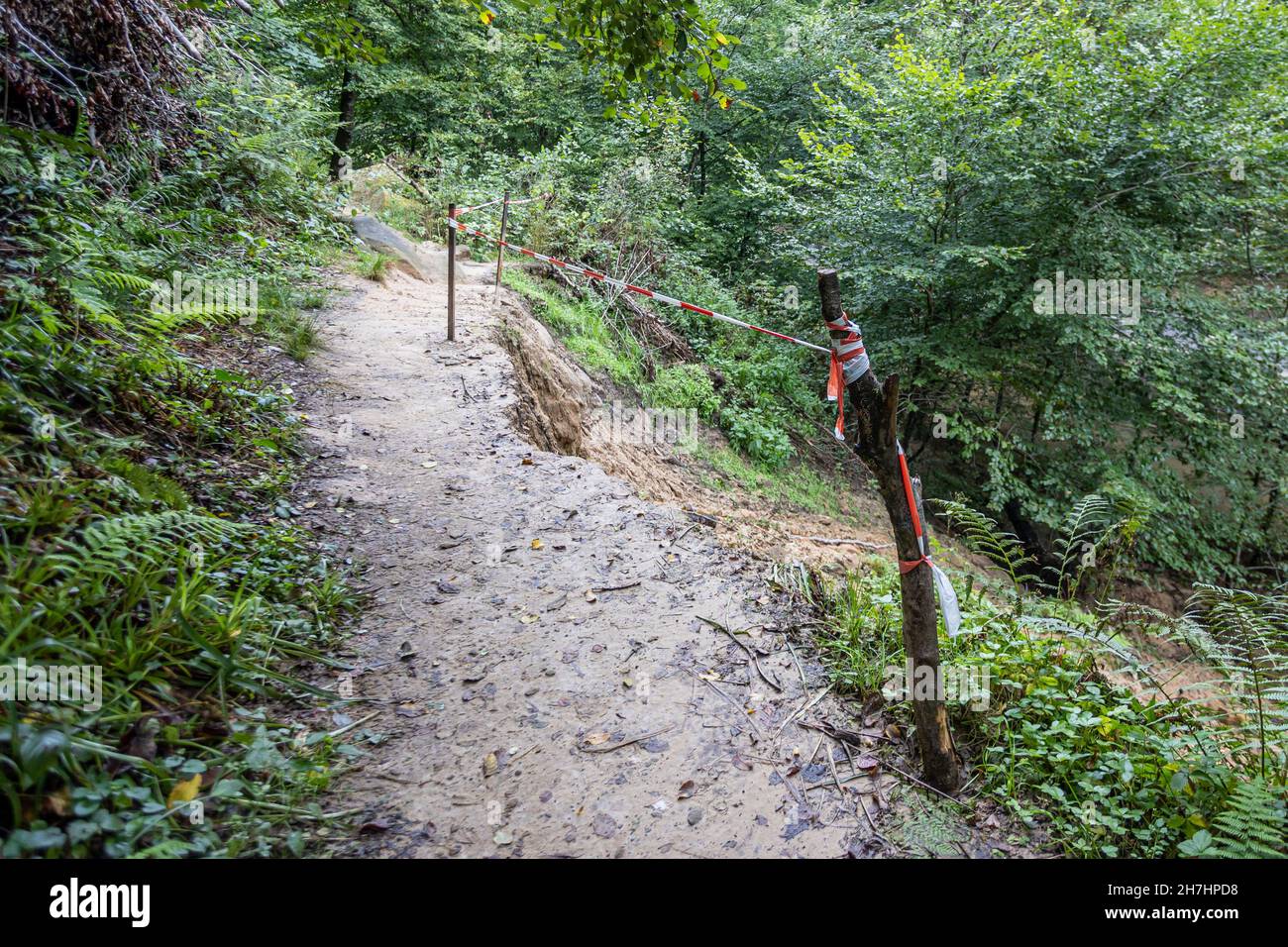 Dirt path damaged by a storm, wooden posts with a white and red tape ...