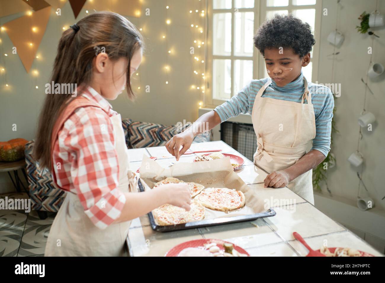 Children making pizza together at the table, they adding ingredients on ...