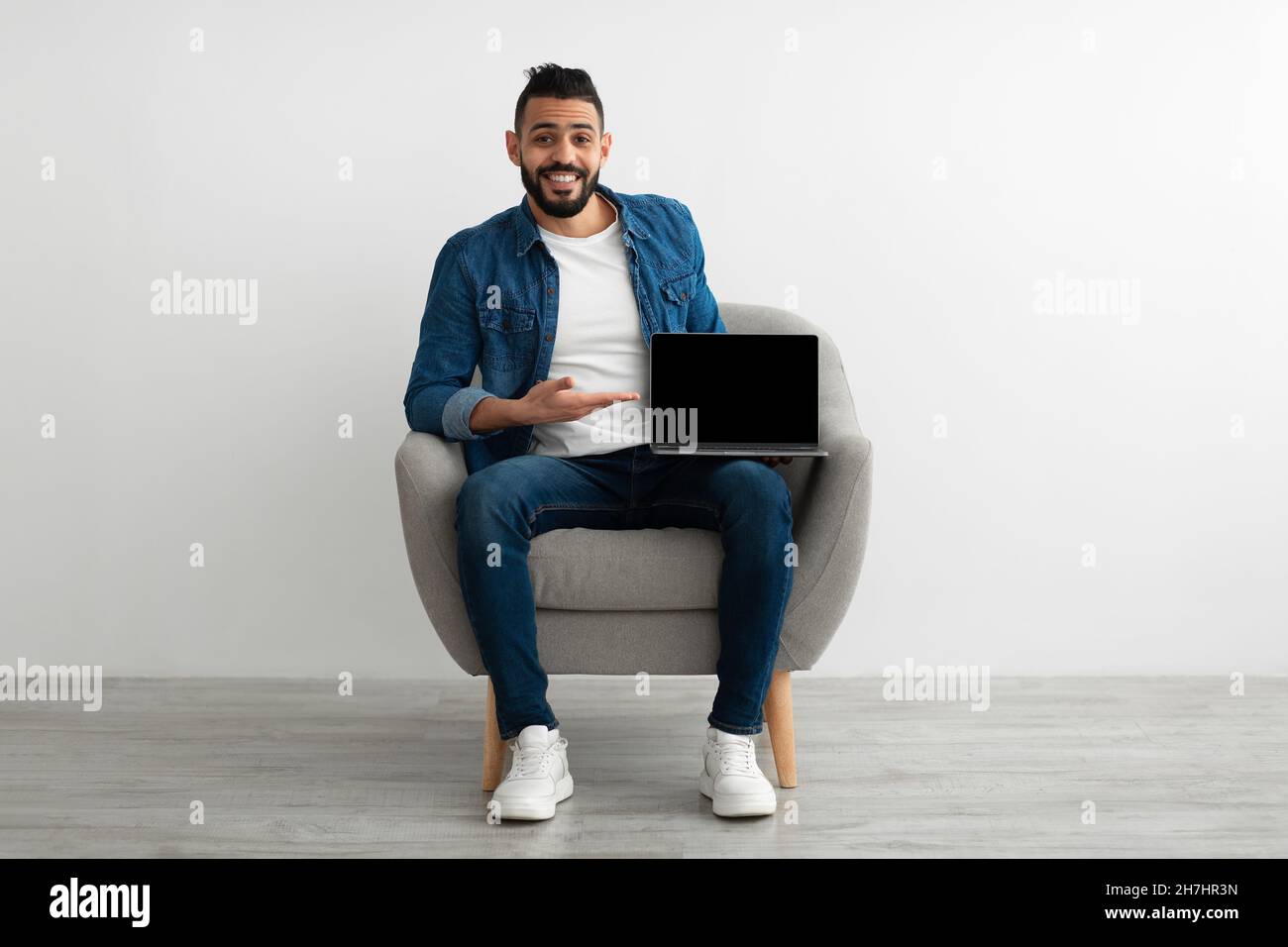 Happy young Arab man demonstrating laptop with empty screen, sitting in ...
