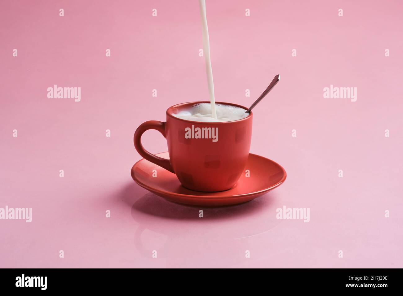 red mug on a pink background with reflection. Pouring milk into the cup ...