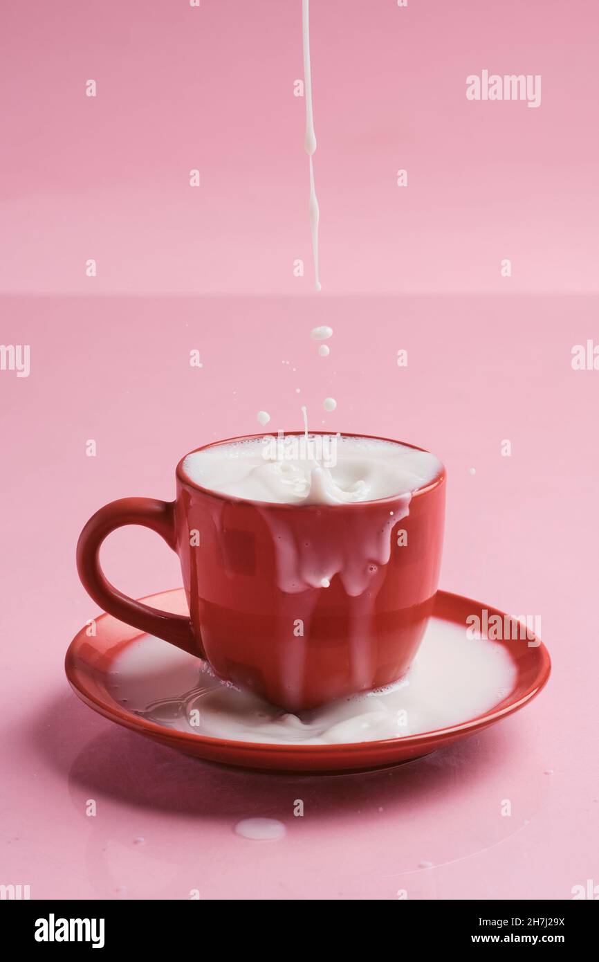 red mug on a pink background with reflection. Pouring milk into the cup ...