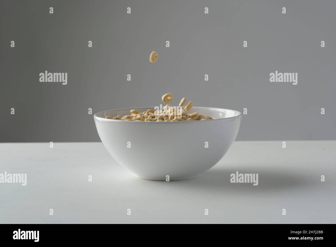 Loop cereals falling into a white bowl on a white table with grey ...