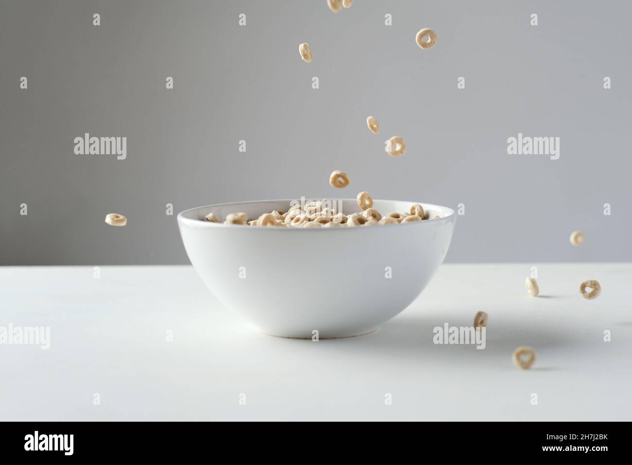 Loop cereals falling into a white bowl on a white table with grey ...