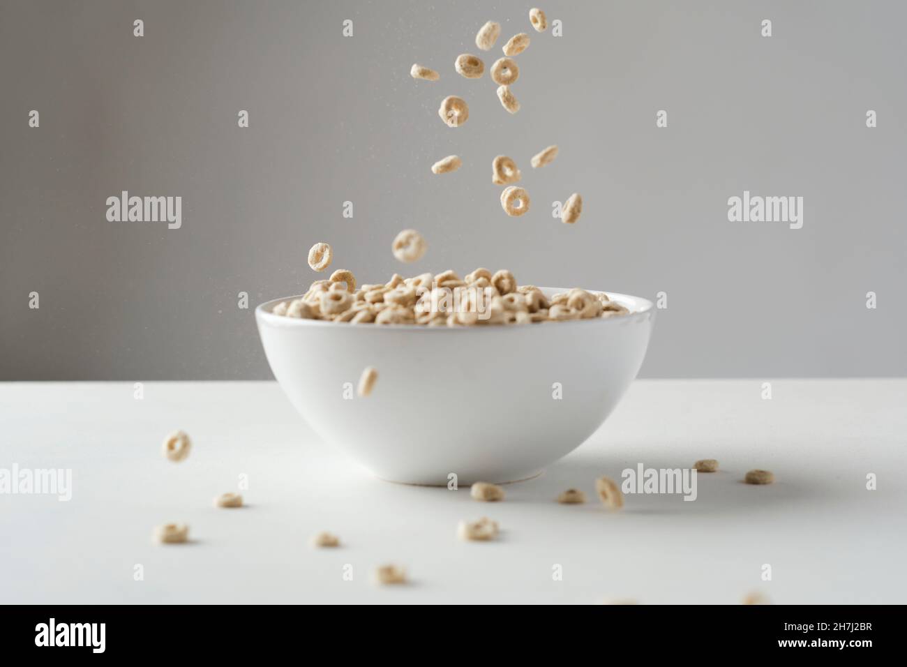 Loop cereals falling into a white bowl on a white table with grey ...