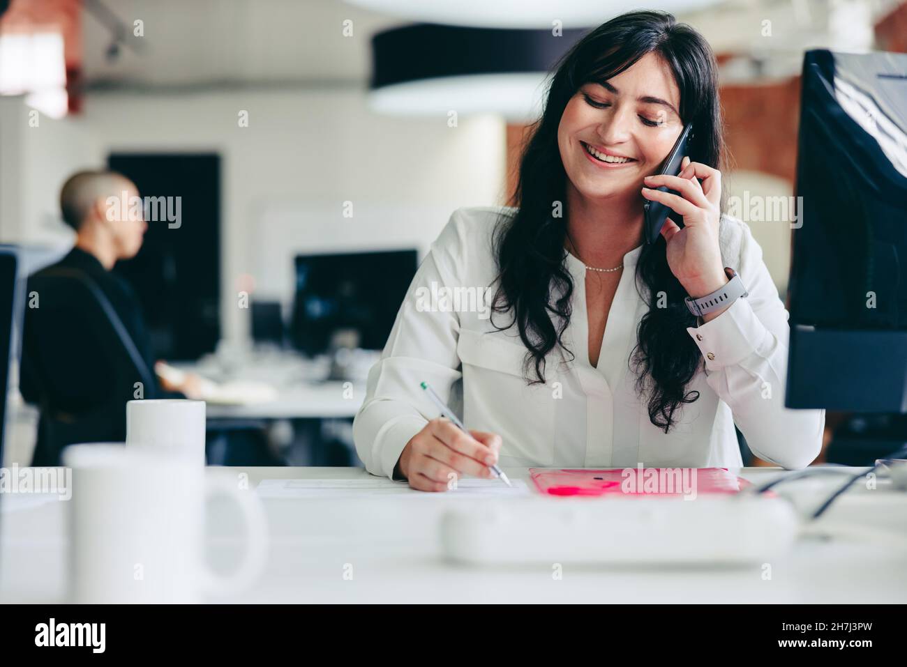 Happy businesswoman making business plans while speaking on a phone ...