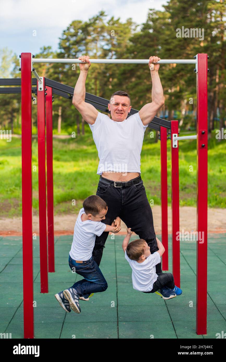 Caucasian man and two boys doing exercises outdoors. The father pulls ...