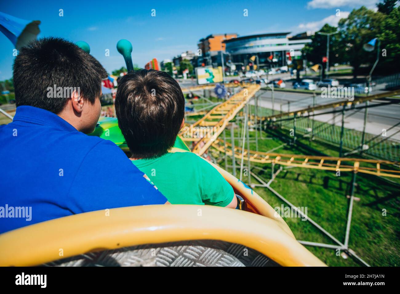 Teenager and his kid brother riding a roller coaster at a theme park ...