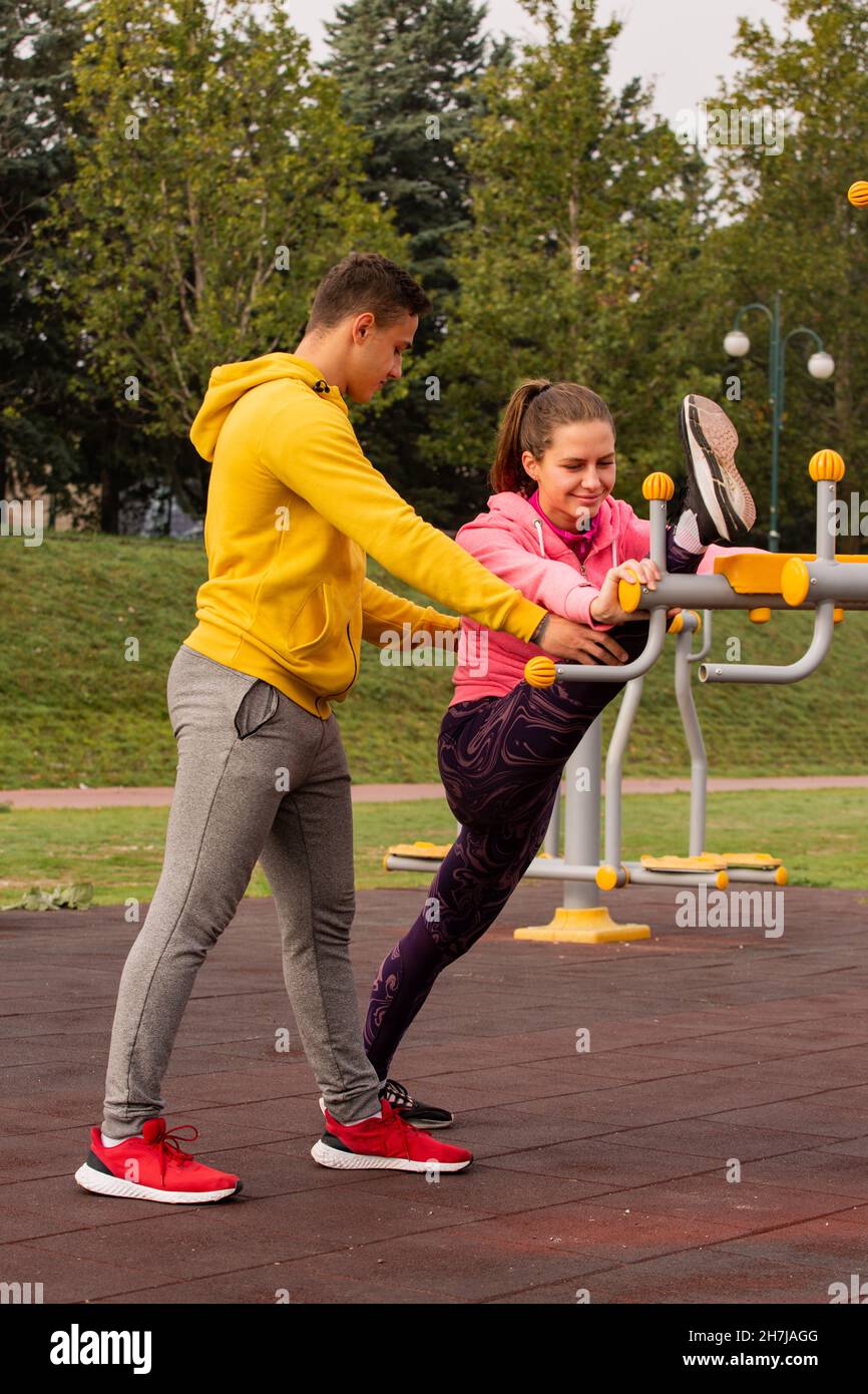 Handsome guy is helping his girlfriend to stretch her legs on the bars ...