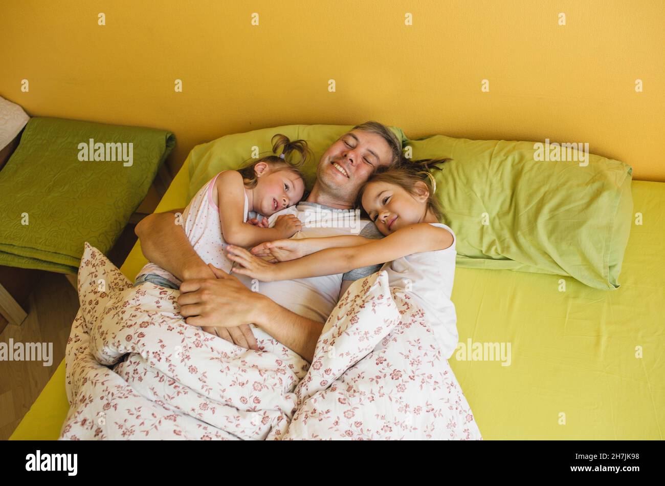 a happy father is lying in bed with two young daughters Stock Photo - Alamy