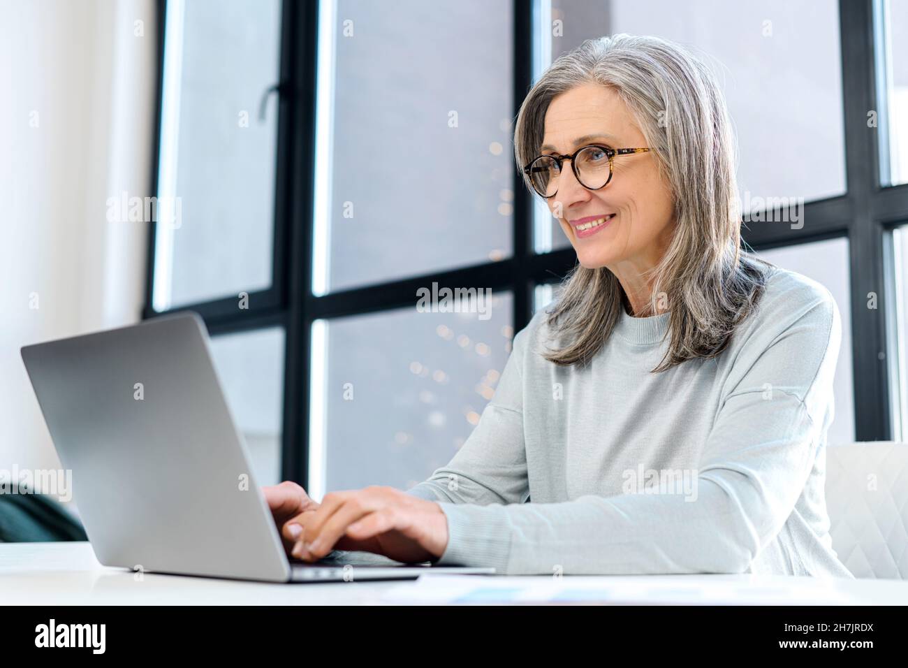 Middle-aged woman sitting on the desk in the office and chatting online ...