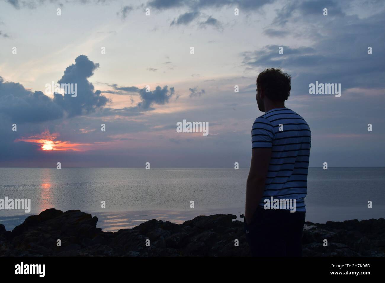 Landscape photo of a man or person watching ocean or sea at sunset or ...