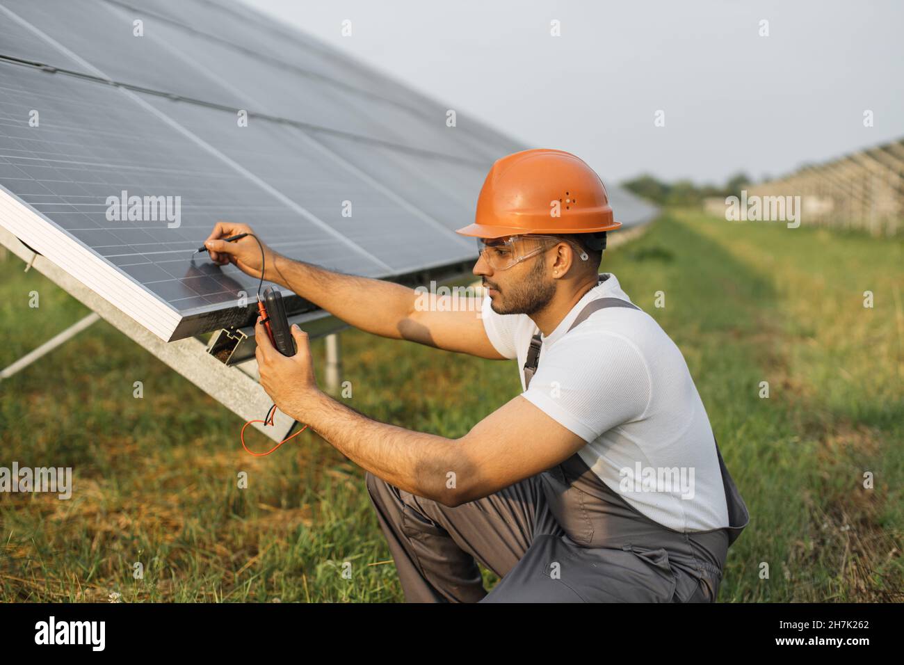 Competent technician in safety helmet and glasses measuring amperage of ...