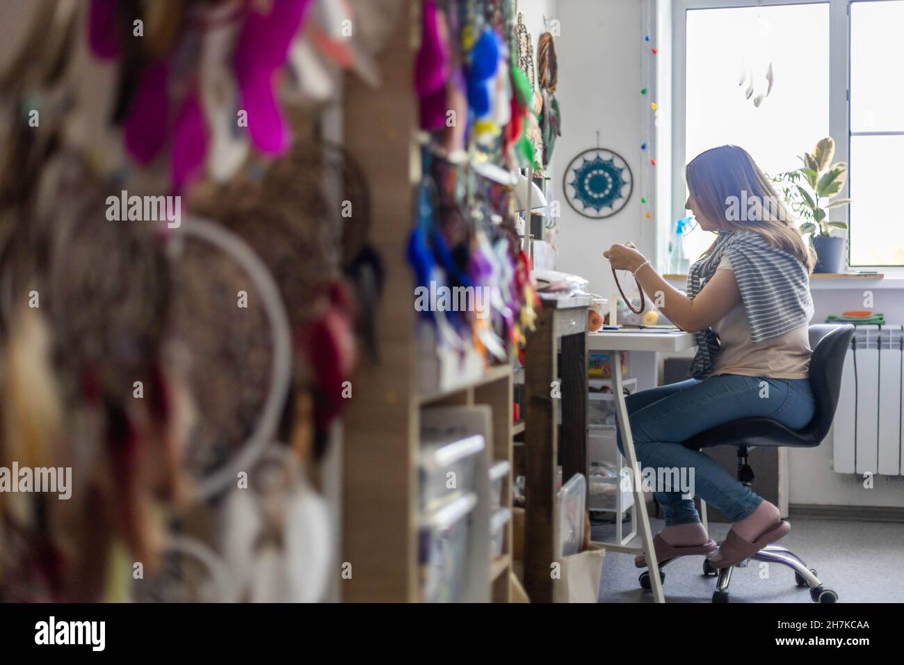 Female master creating Dreamcatcher working at workshop with feathers ...