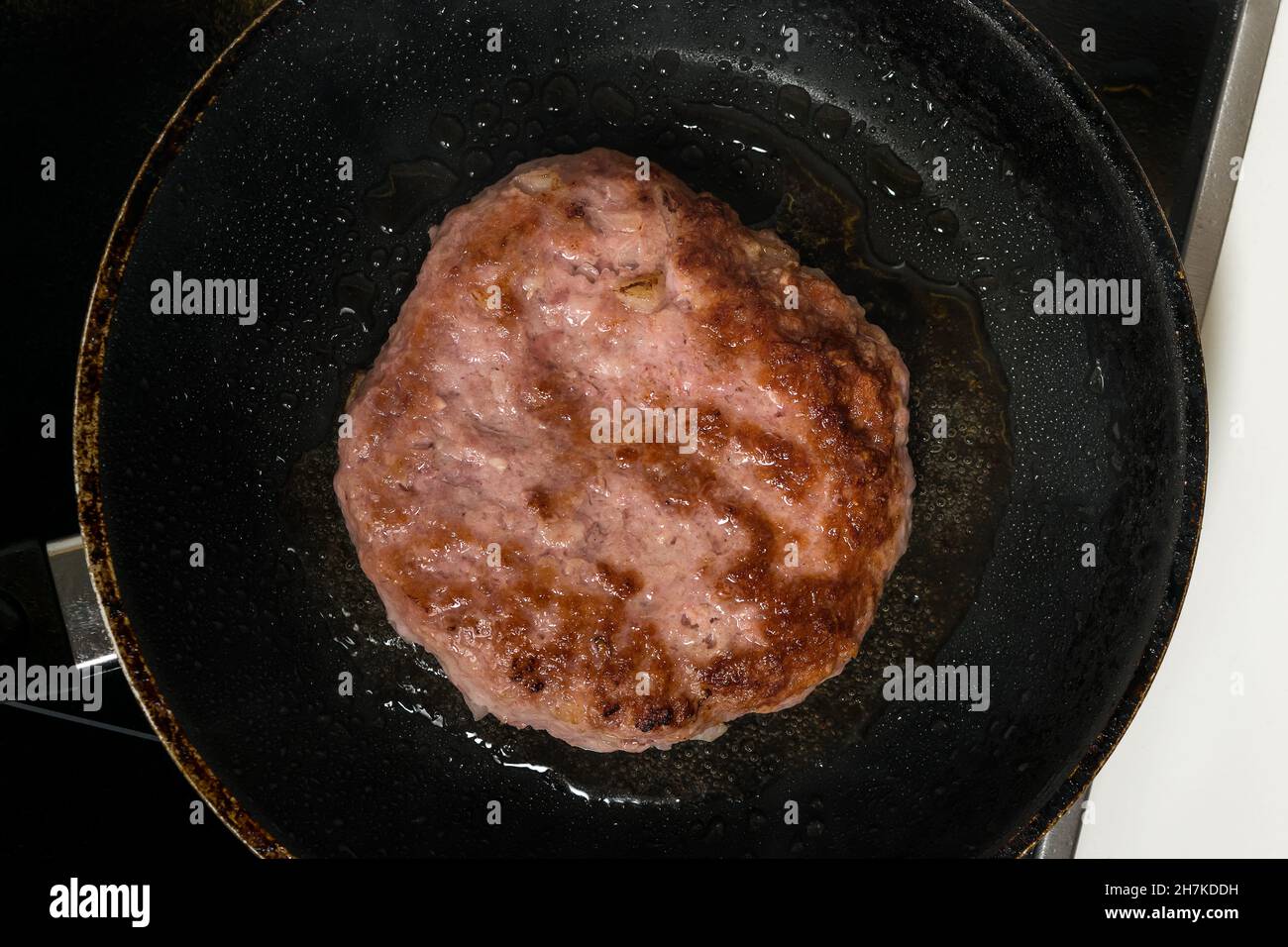 Meat burger being shallow fried in oil on a frying pan, close up. Top ...