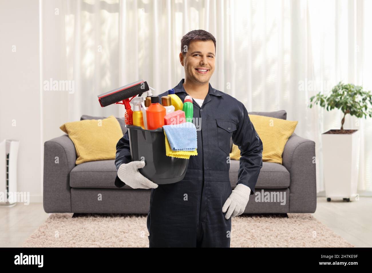Male cleaner in a uniform holding a bucket of cleaning supplies in a ...