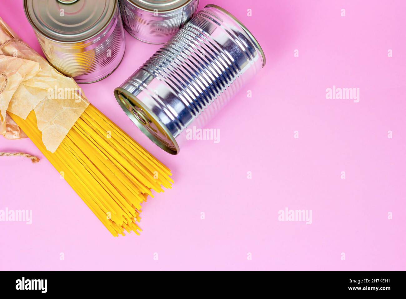 Tinned food, metal cans and yellow spaghetti pasta on pink background ...