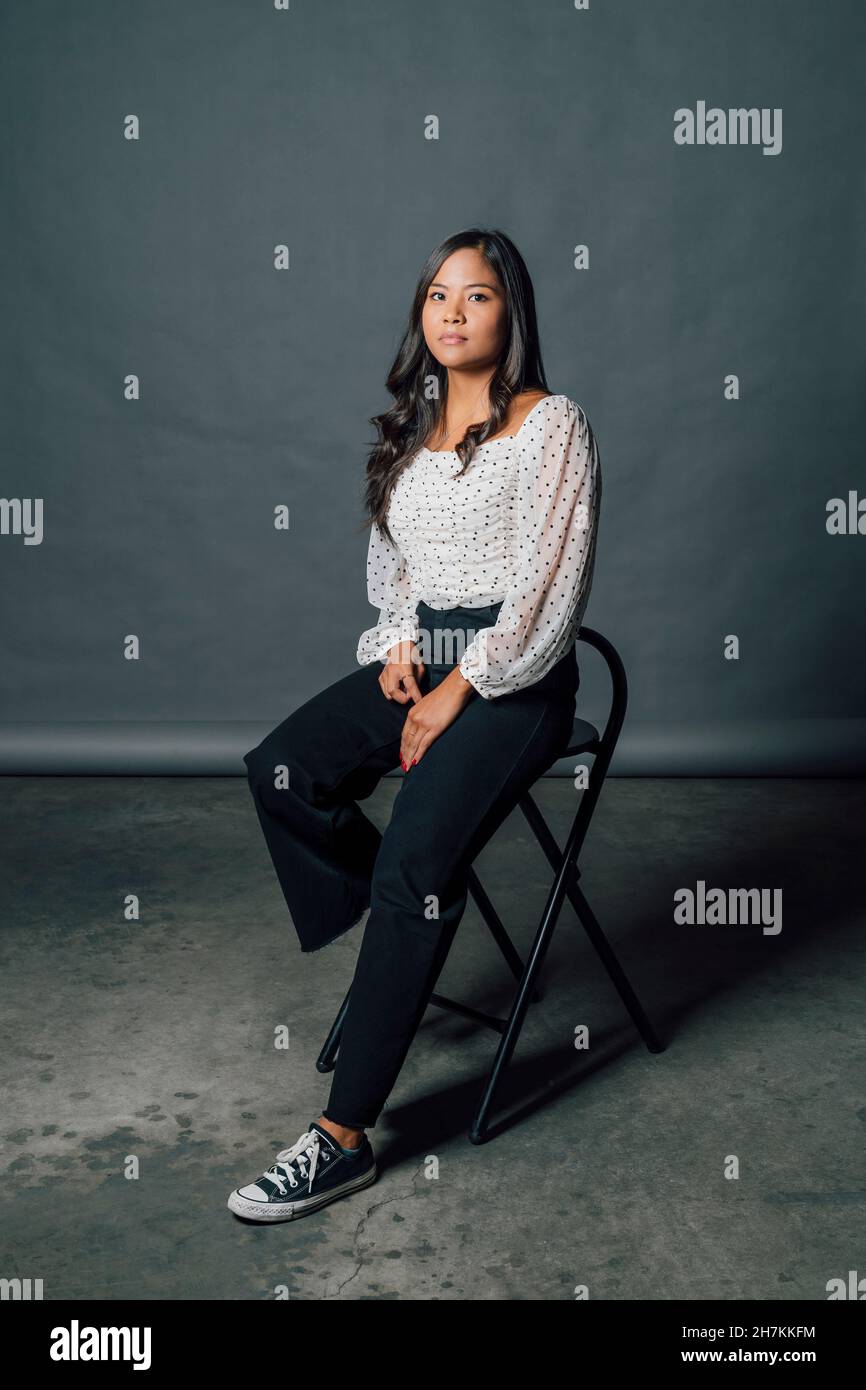 Beautiful serious woman sitting on chair in front of gray backdrop ...