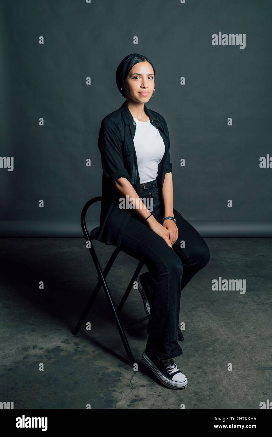 Beautiful woman sitting on chair in front of gray backdrop Stock Photo ...