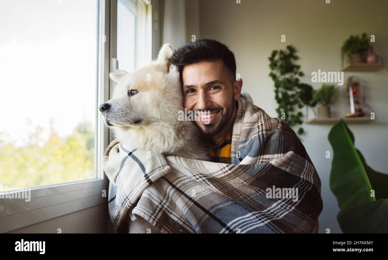 Happy man embracing Akita dog by window Stock Photo - Alamy