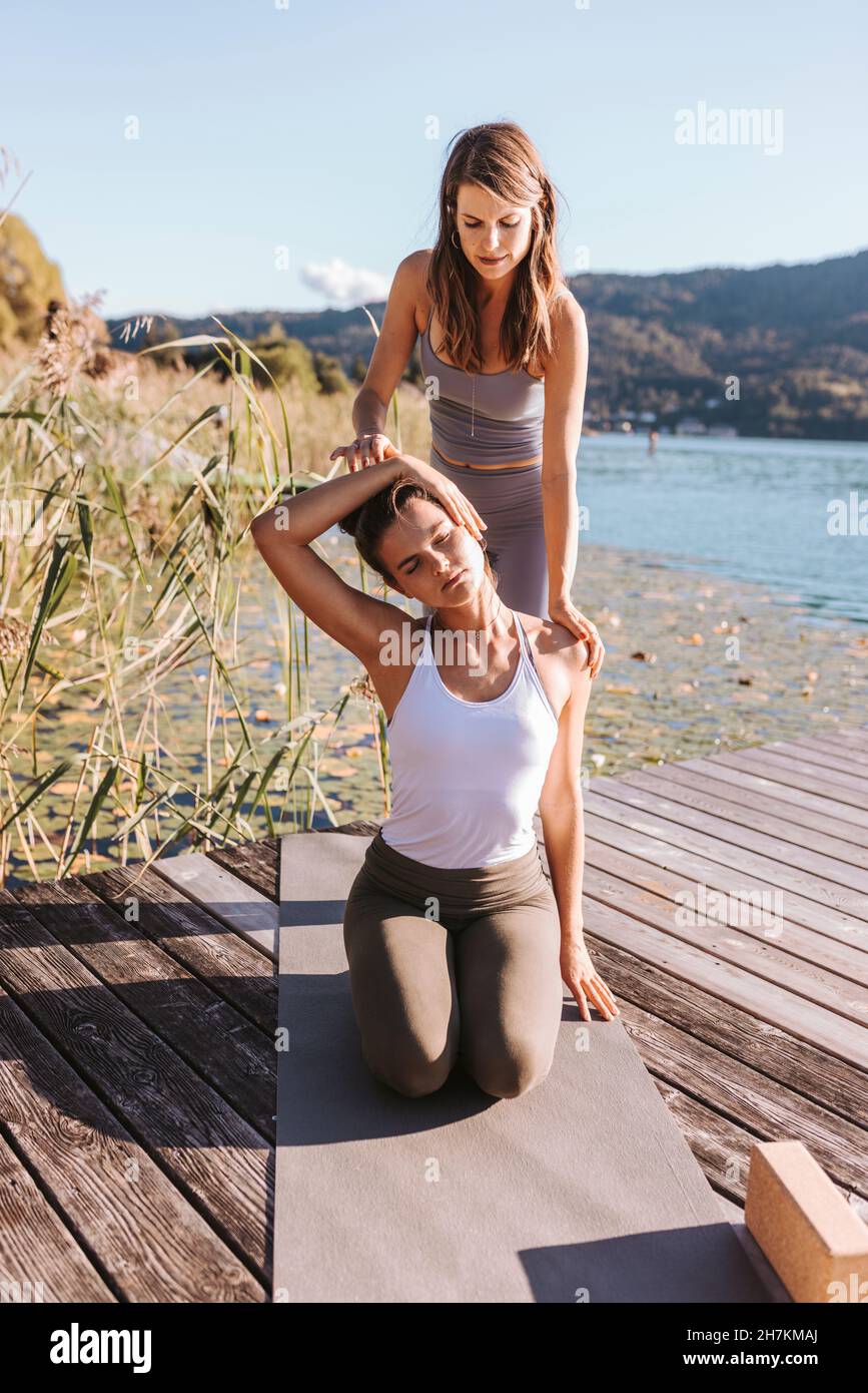 Female instructor assisting women while stretching neck during yoga ...