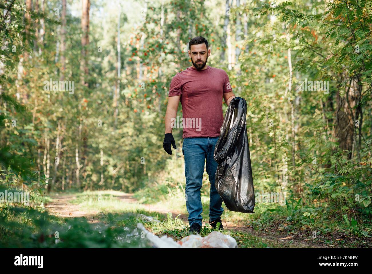 Male climate activist with garbage bag walking in forest Stock Photo ...