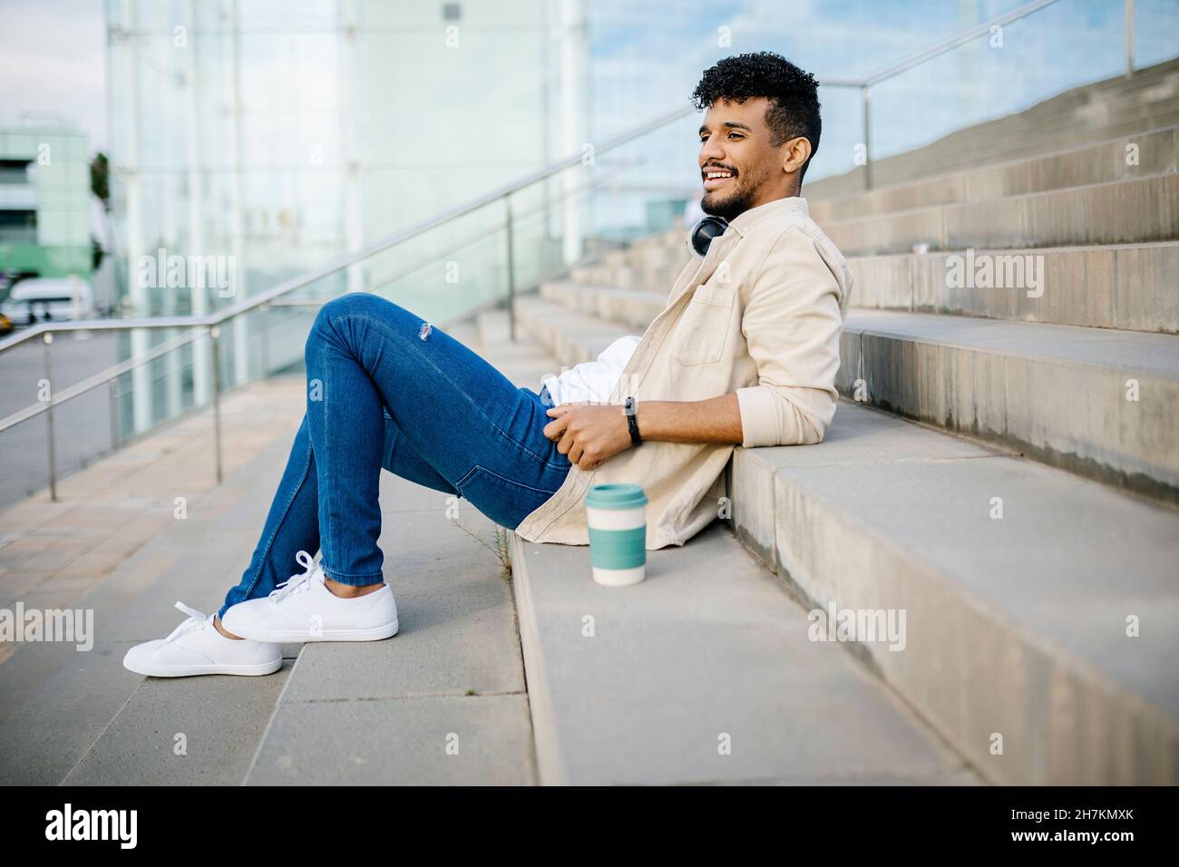 Smiling man sitting by paper coffee cup on steps Stock Photo - Alamy