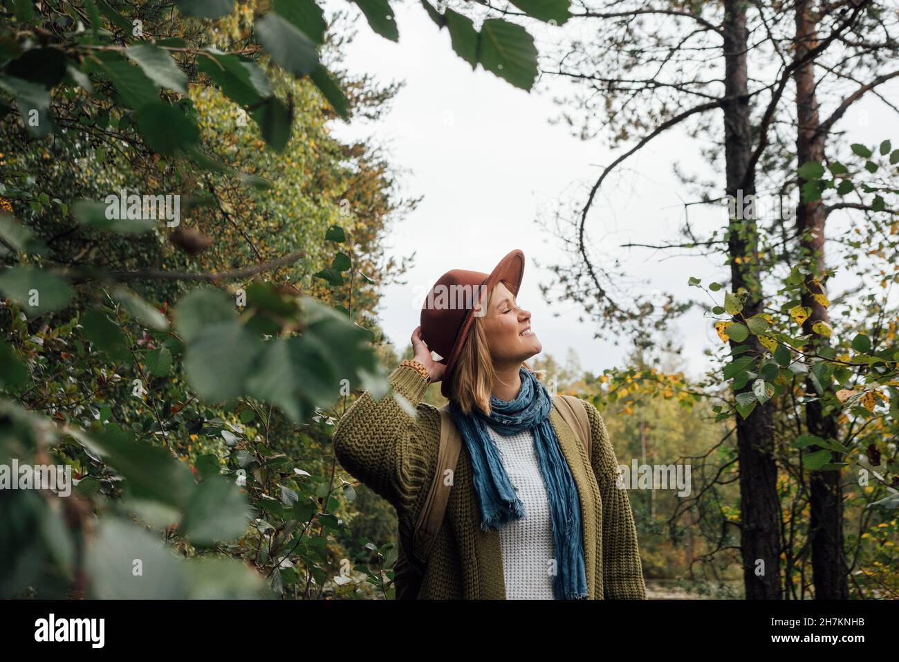 Woman adjusting hat while standing with eyes closed in forest Stock ...