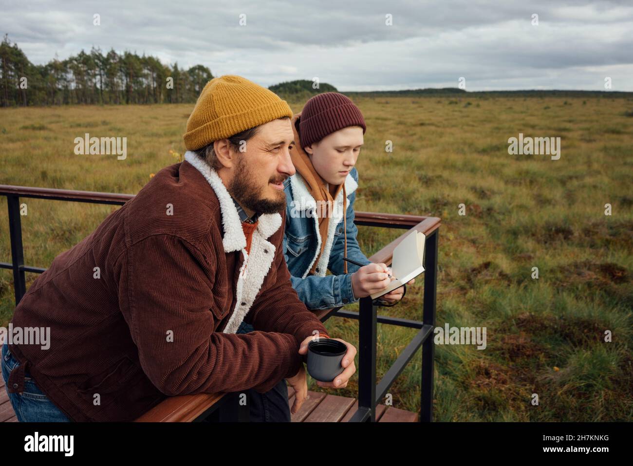 Boy writing in diary while leaning on railing with father Stock Photo ...