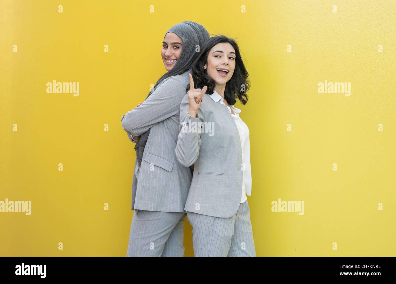 Cheerful female colleagues cheering in front of yellow wall Stock Photo ...