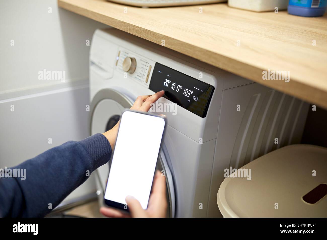 Woman operating washing machine through smart phone in utility room at ...