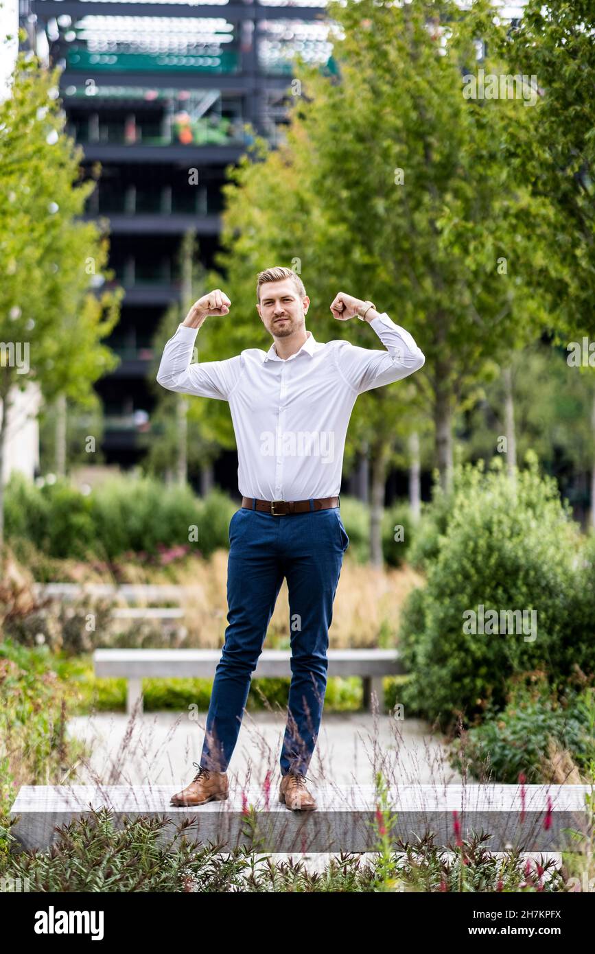 Businessman flexing muscles while standing on bench Stock Photo - Alamy