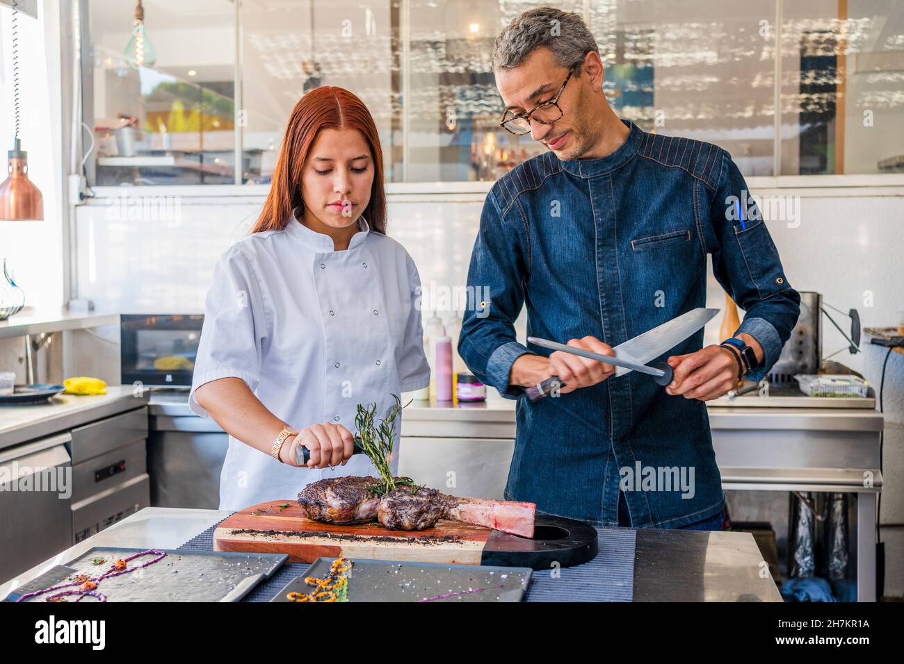 Female chef cutting meat by male colleague in kitchen Stock Photo - Alamy