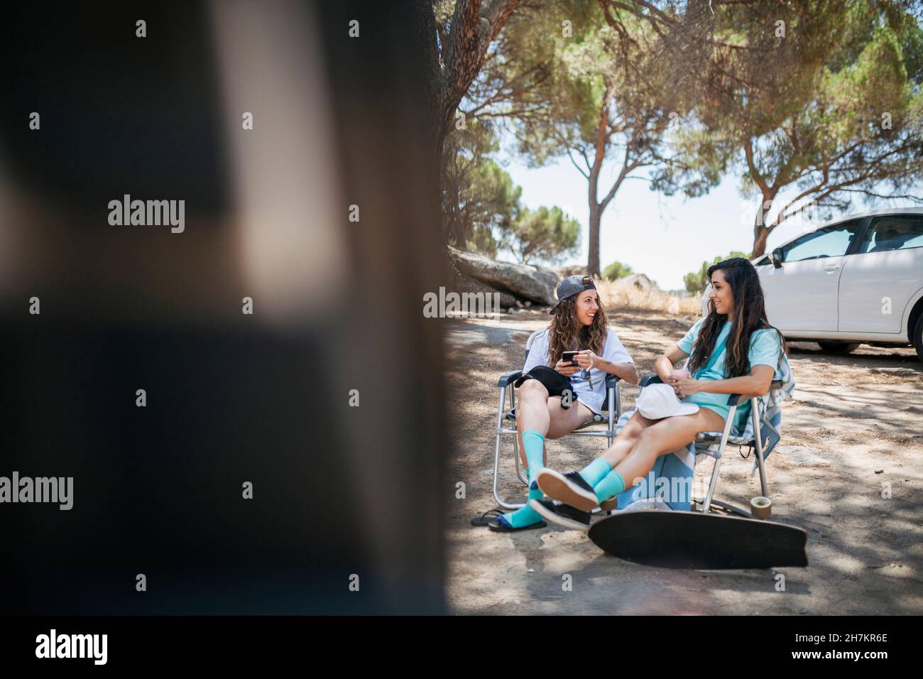 Smiling female friends talking while sitting on chair Stock Photo - Alamy