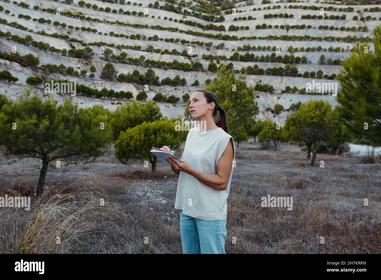 Female scientist contemplating while writing in book at filed Stock ...