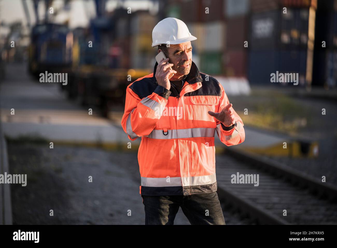 Mature male dock worker gesturing while talking on smart phone by ...