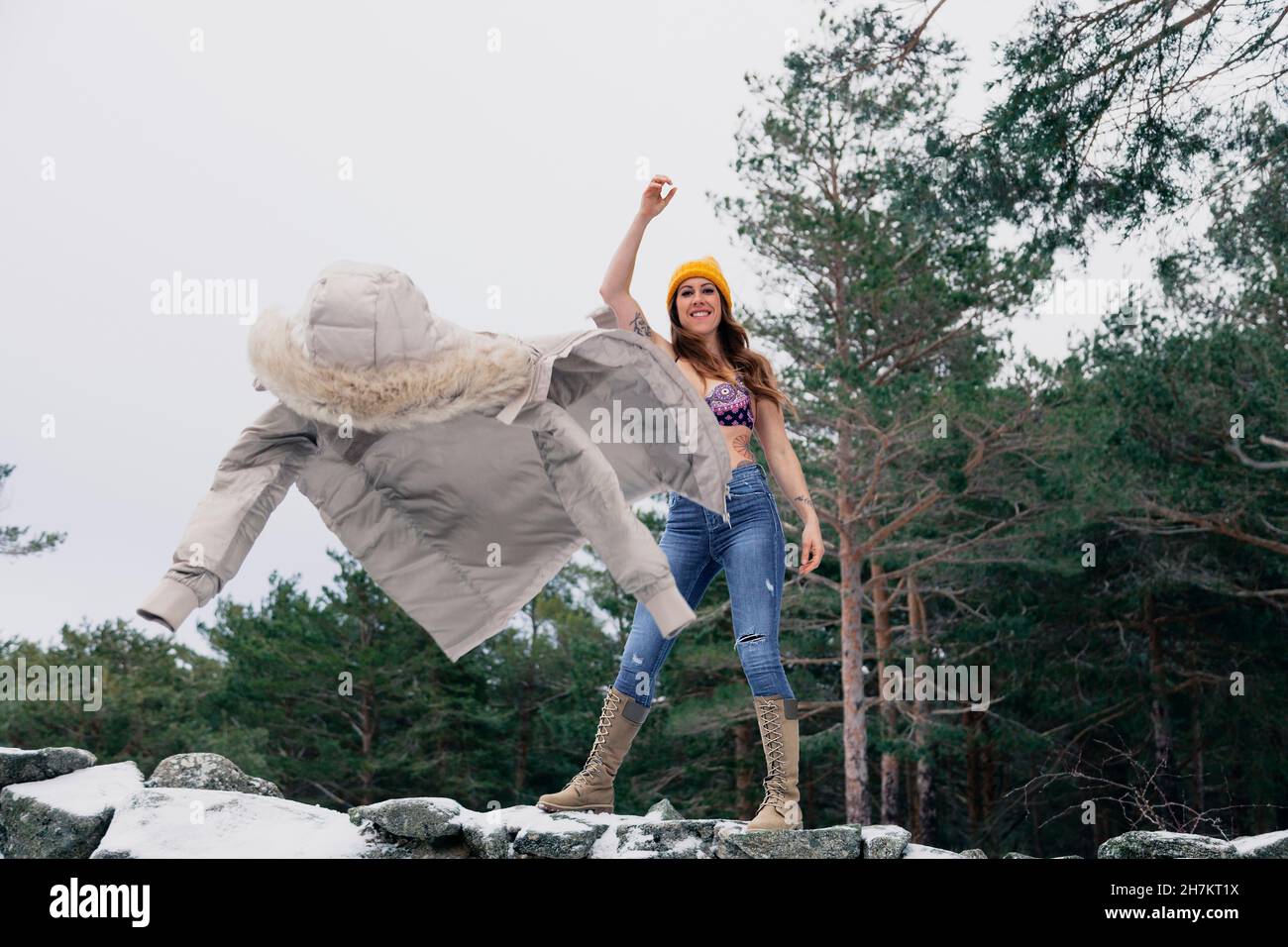 Carefree woman throwing winter coat while standing on rock in winter ...