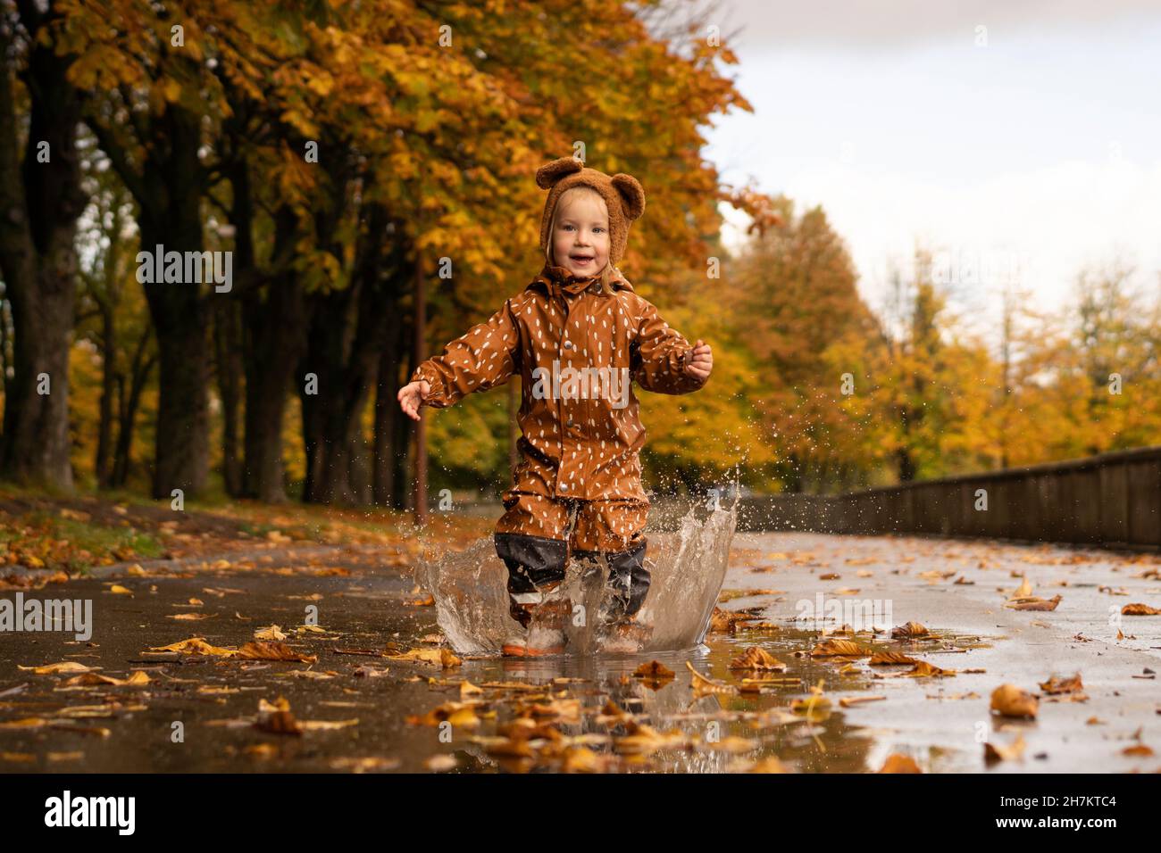 Girl wearing brown raincoat splashing in puddle on road Stock Photo - Alamy