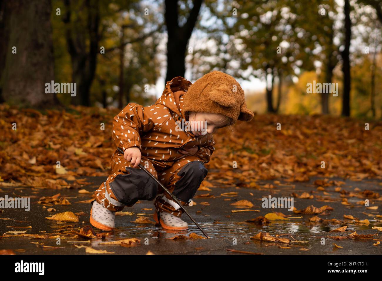 Girl holding stick while playing at puddle Stock Photo - Alamy